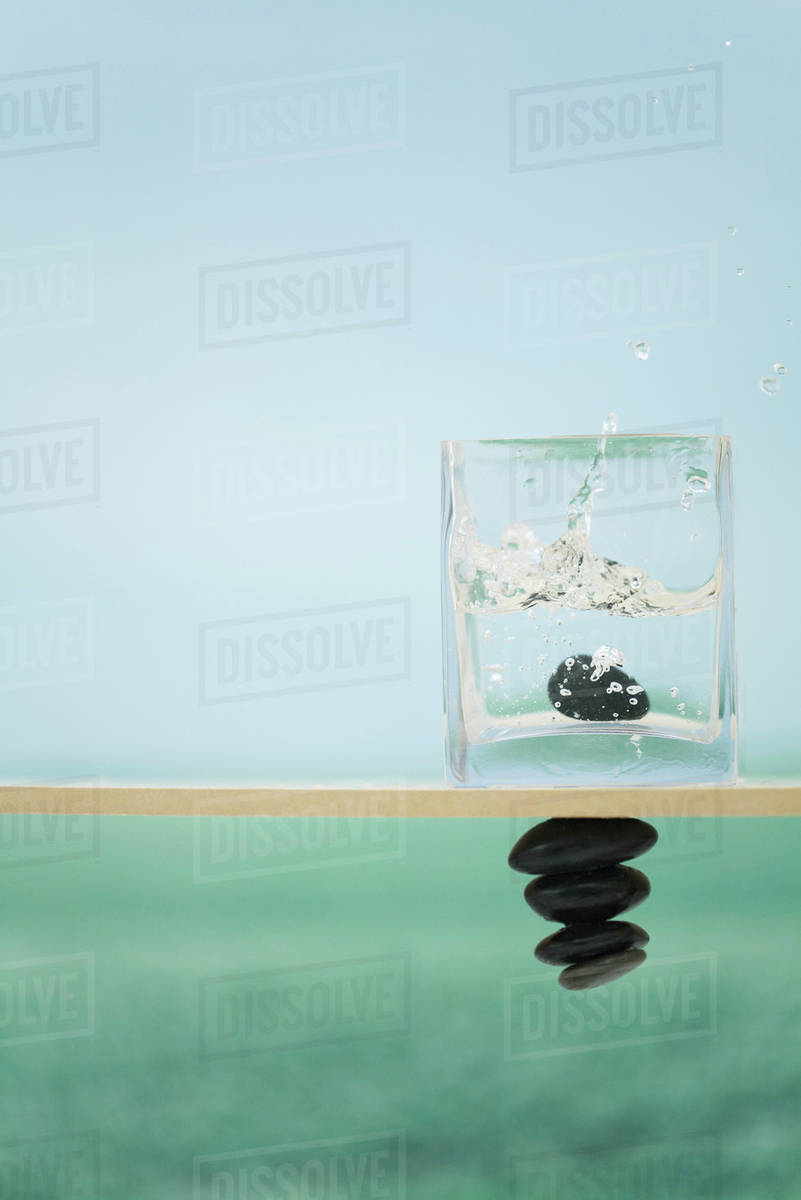 Stone falling in glass container, creating water splash, pile of stones ...
