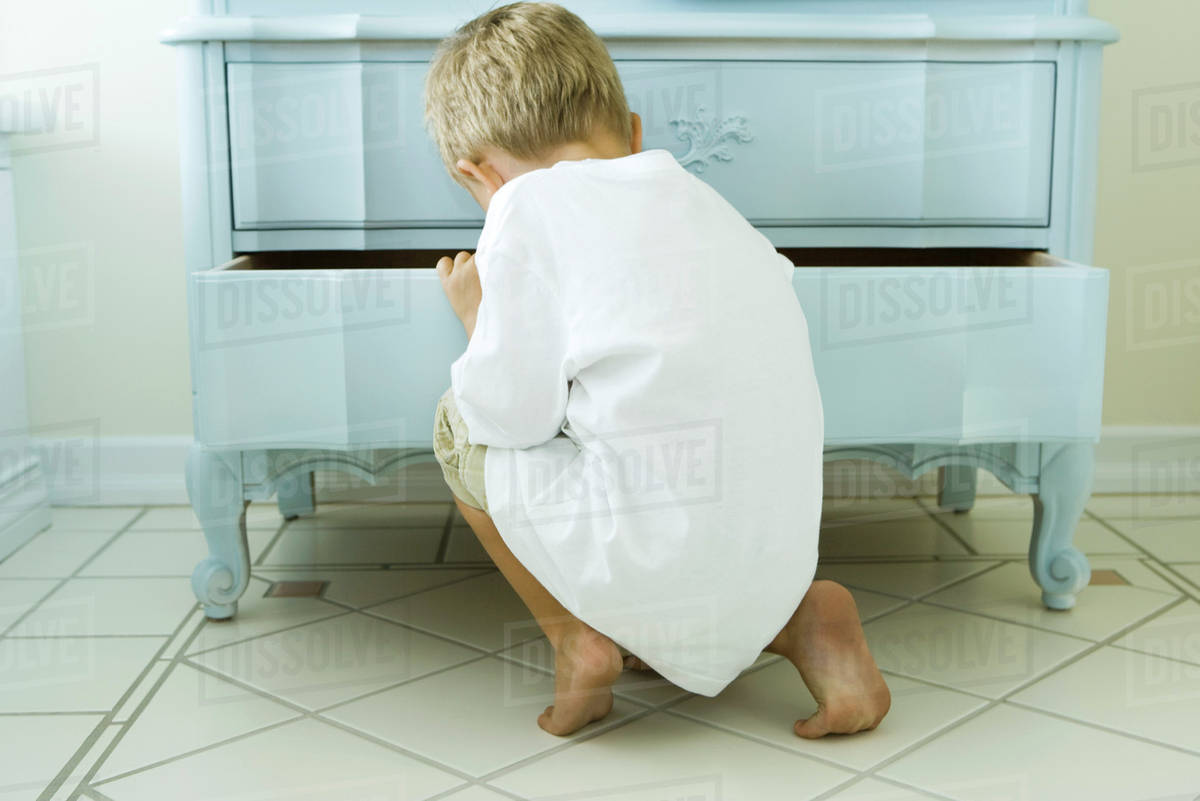 Boy crouching, snooping in chest of drawers - Stock Photo - Dissolve