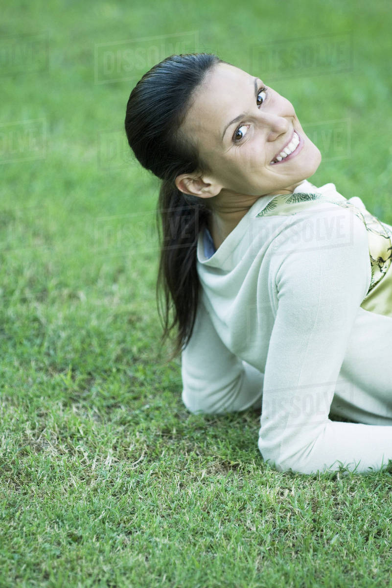 Woman reclining on grass, smiling over shoulder at camera - Royalty ...