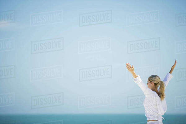Young woman standing with arms out, ocean horizon in background ...