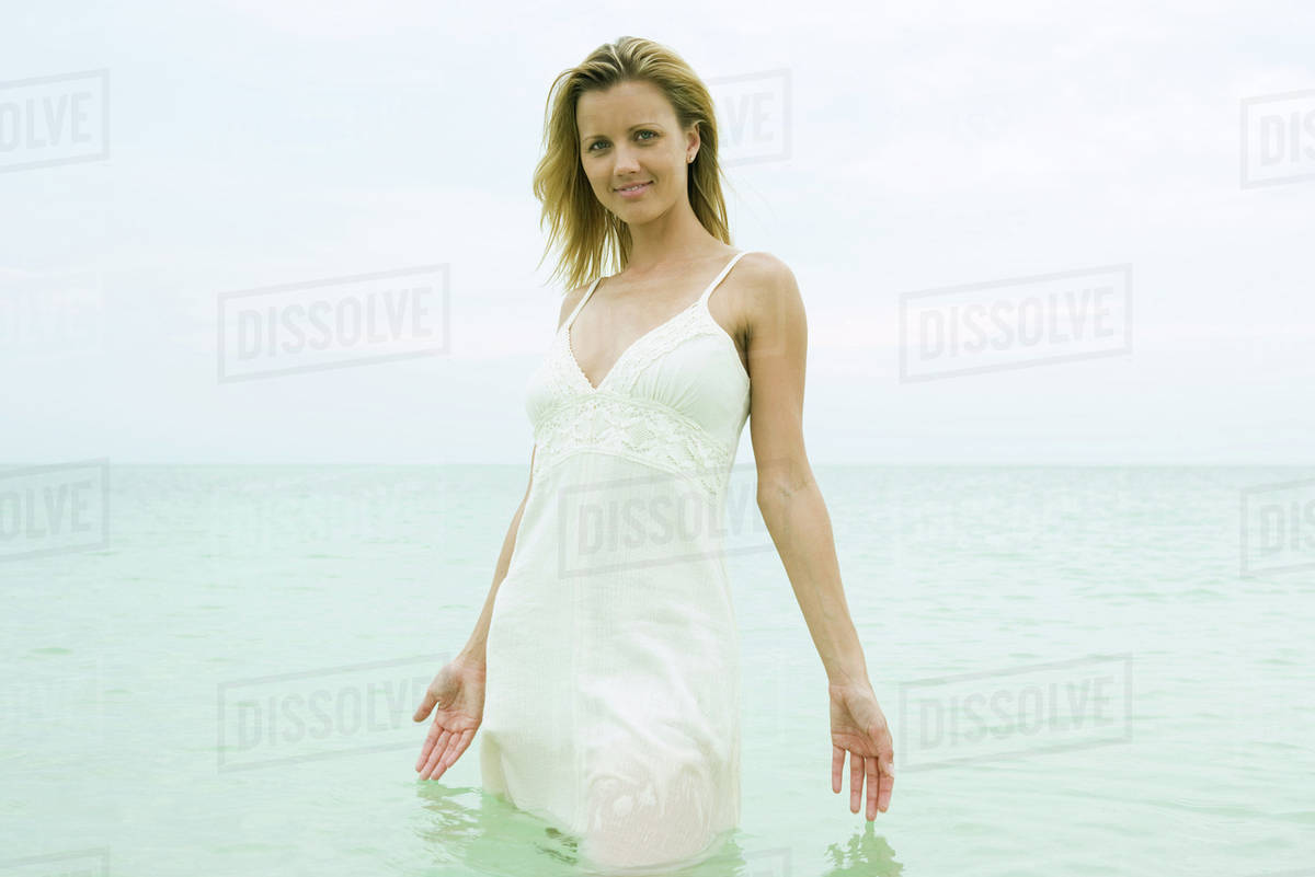 Woman standing thigh deep in ocean, touching surface of water, smiling ...