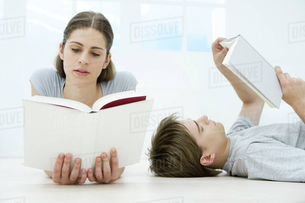 Couple reading books, man lying on back, woman lying on stomach ...