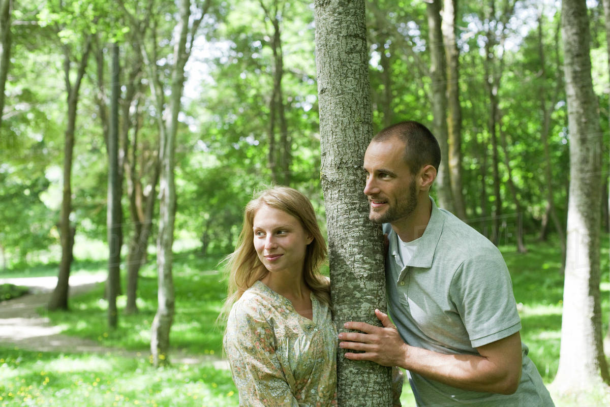 Couple leaning against tree trunk - Stock Photo - Dissolve