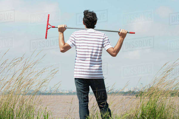 Man holding rake on shoulders, looking at city skyline from afar, rear ...