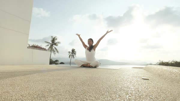 Asian woman sitting in turkish pose Sukhasana on outdoor balcony with ...