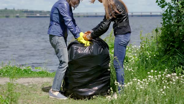 Two beautiful caucasian girls picking up a garbage in bag. Young women ...