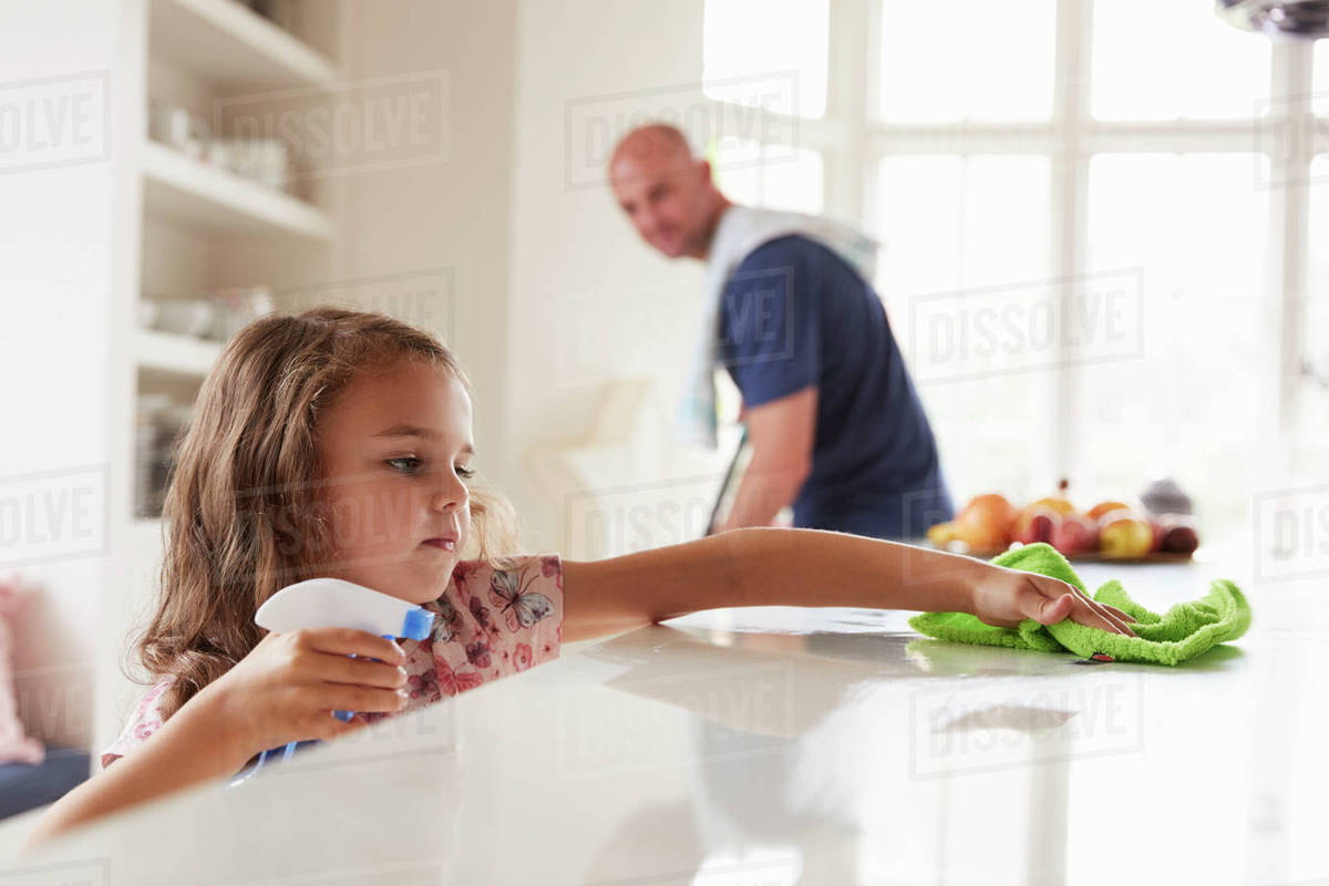 Young girl cleaning kitchen worktop, dad in background - Royalty-free ...