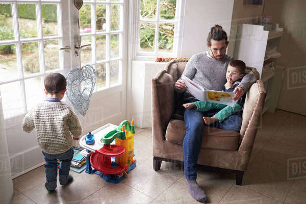 Father sitting in chair at home reading story to sons - Royalty-free ...