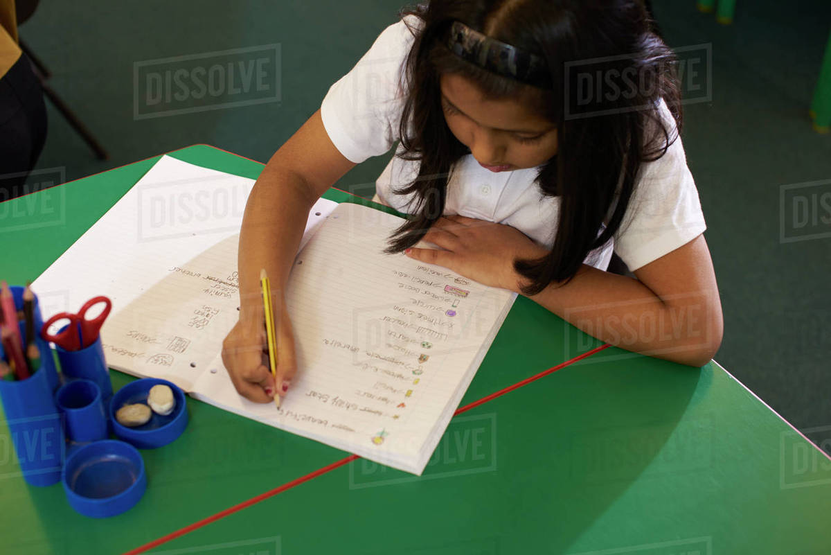 Female pupil working at desk in elementary school classroom - Royalty ...