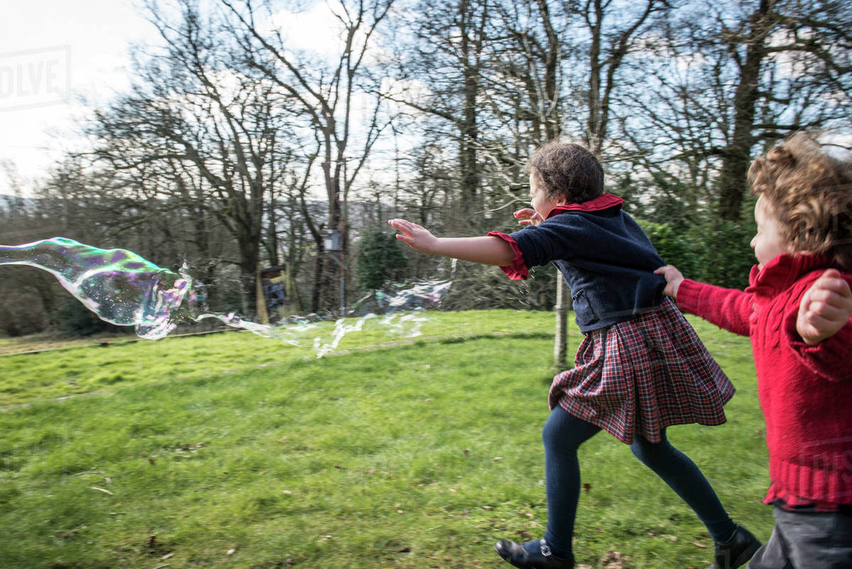 Two young children chasing bubbles around a garden - Stock Photo - Dissolve