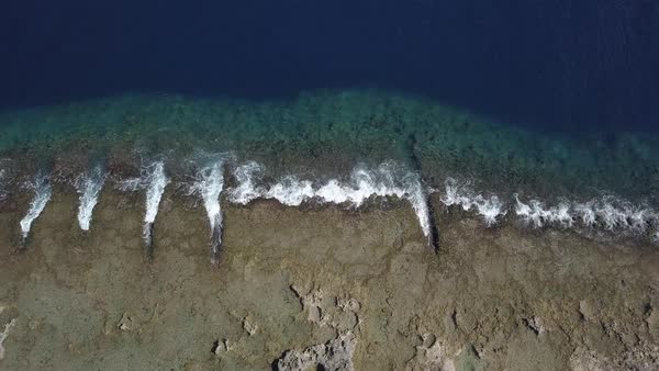 Tracking shot above an eroded coral platform, forming a rugged coast ...