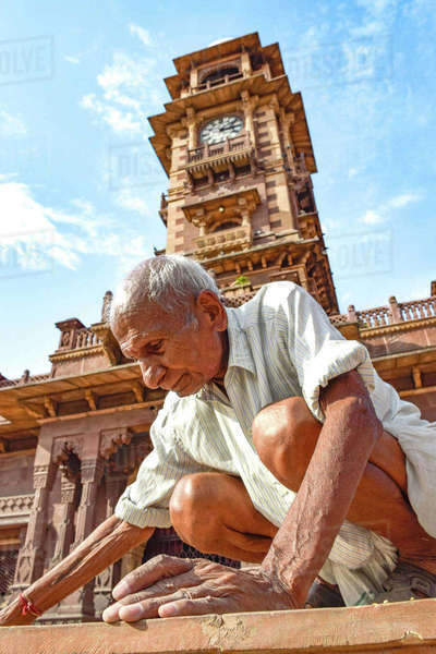 Indian elderly man with white hair under clock square in brown tones ...