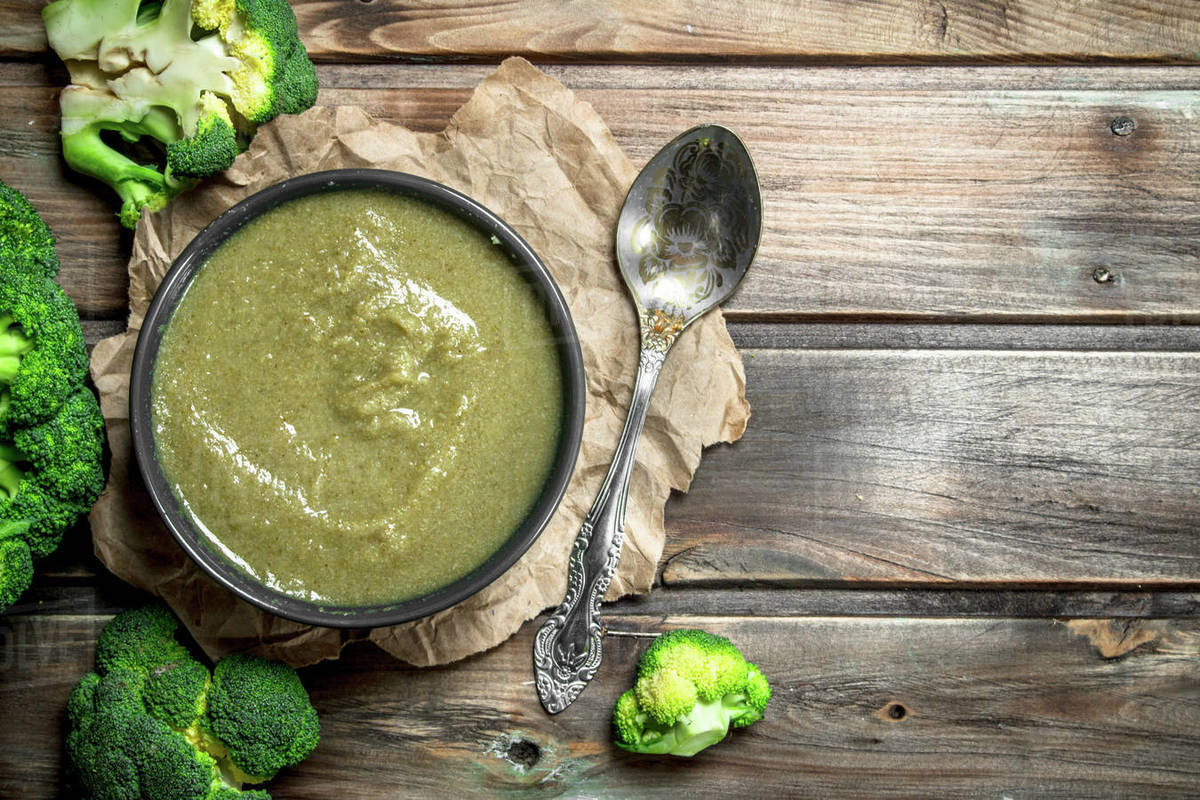 Puree broccoli in a bowl with a spoon. On a wooden background ...
