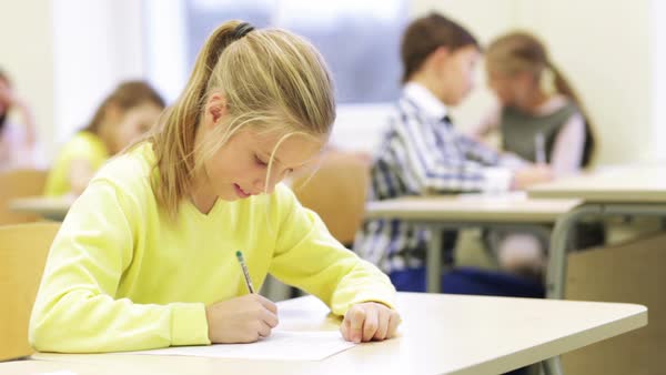 Group of school kids with pens and papers writing test in classroom ...