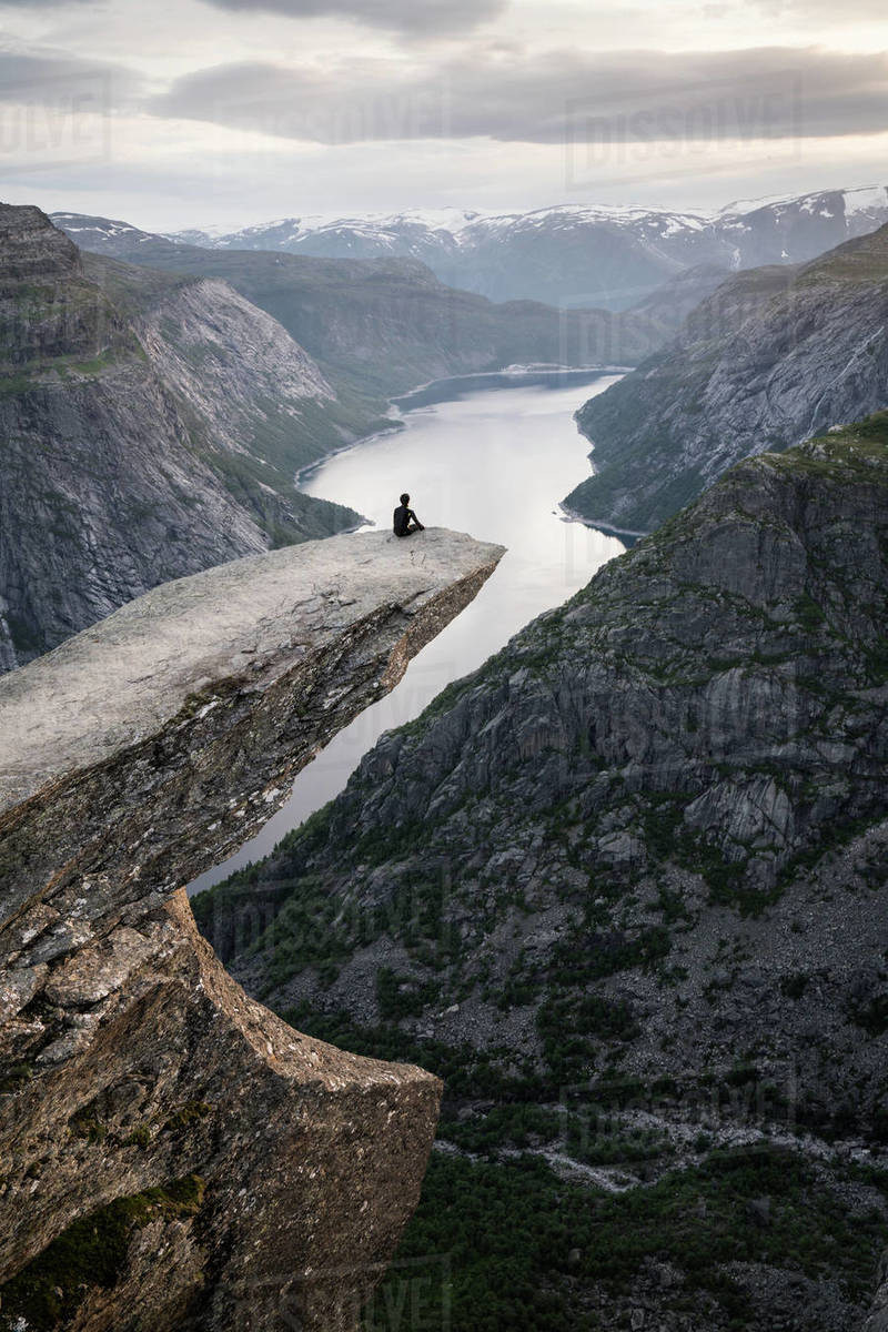 Rear view of a woman looking at view while sitting on top of cliff ...