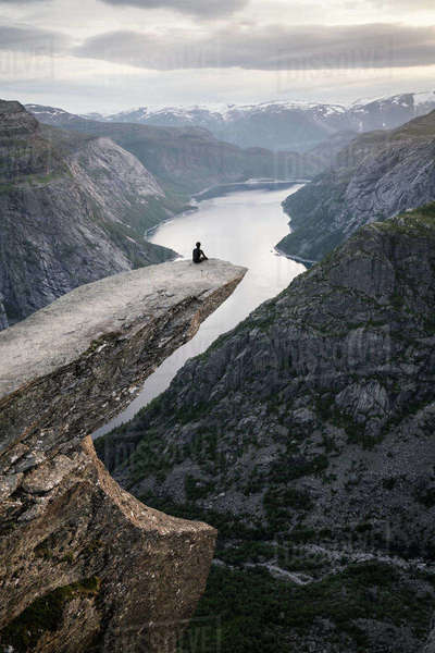Rear view of a woman looking at view while sitting on top of cliff ...