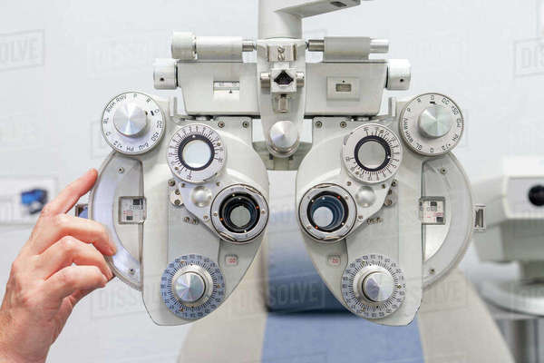 A hand adjusts the lenses on a phoropter, an instrument used by eye ...