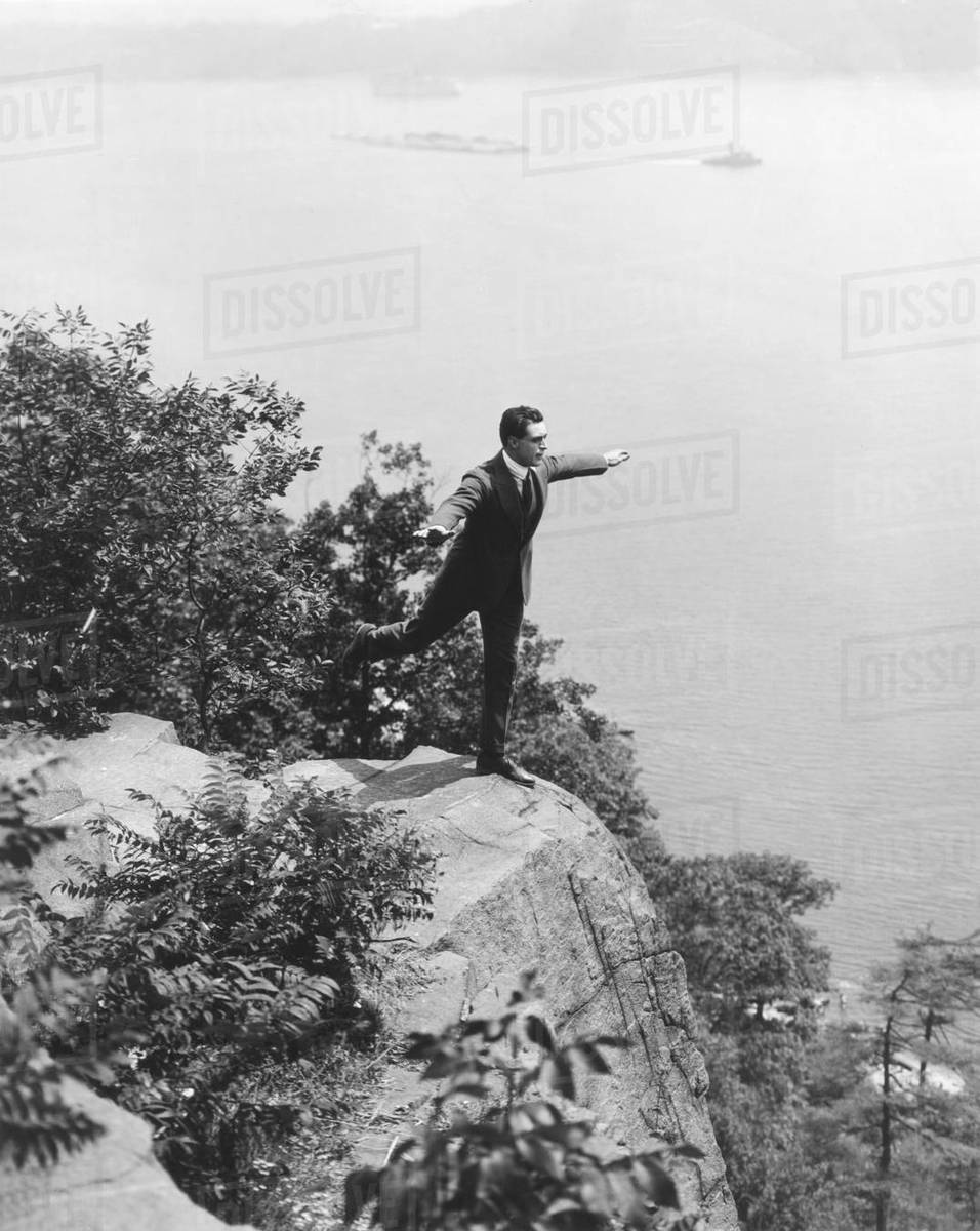 Man standing on one leg at the edge of a cliff - Stock Photo - Dissolve