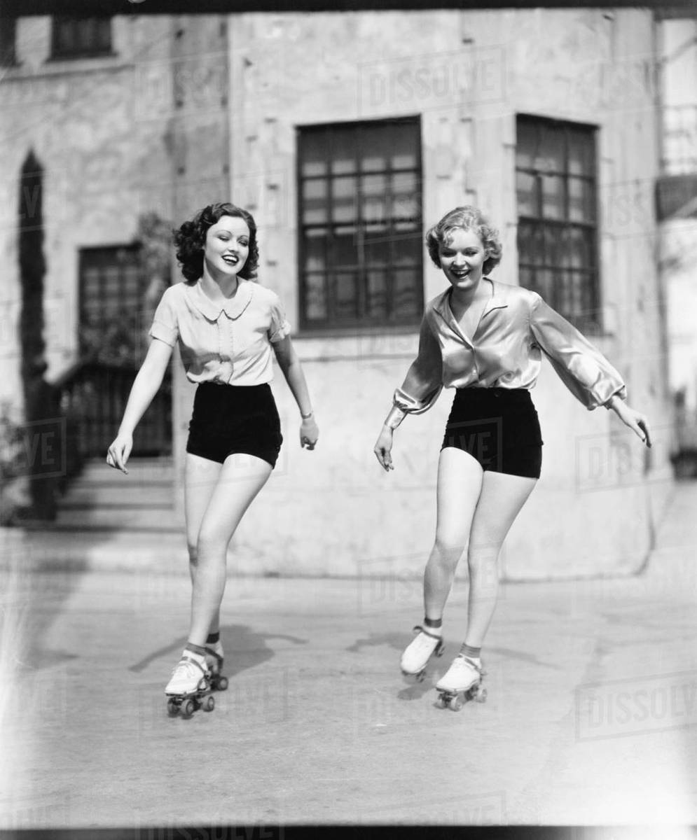 Two young women roller skating on the road and smiling - Royalty-free ...