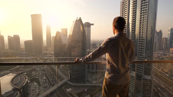 Man standing on balcony and looking over a modern city at sunrise ...