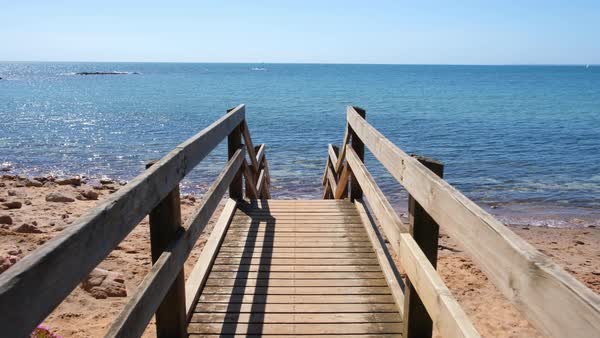 POV forward walk down on wooden stairs leading to secluded ocean beach ...