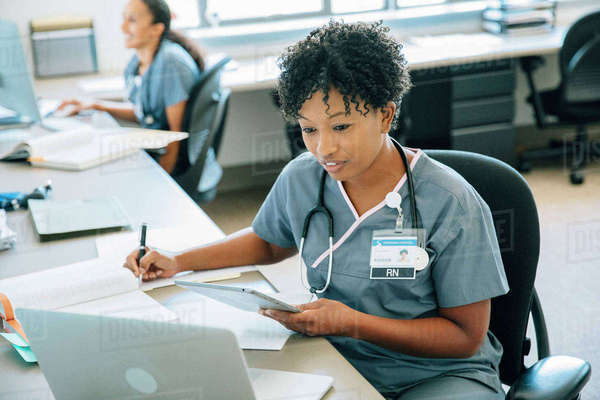 Nurse holding digital tablet and writing on paperwork - Royalty-free ...