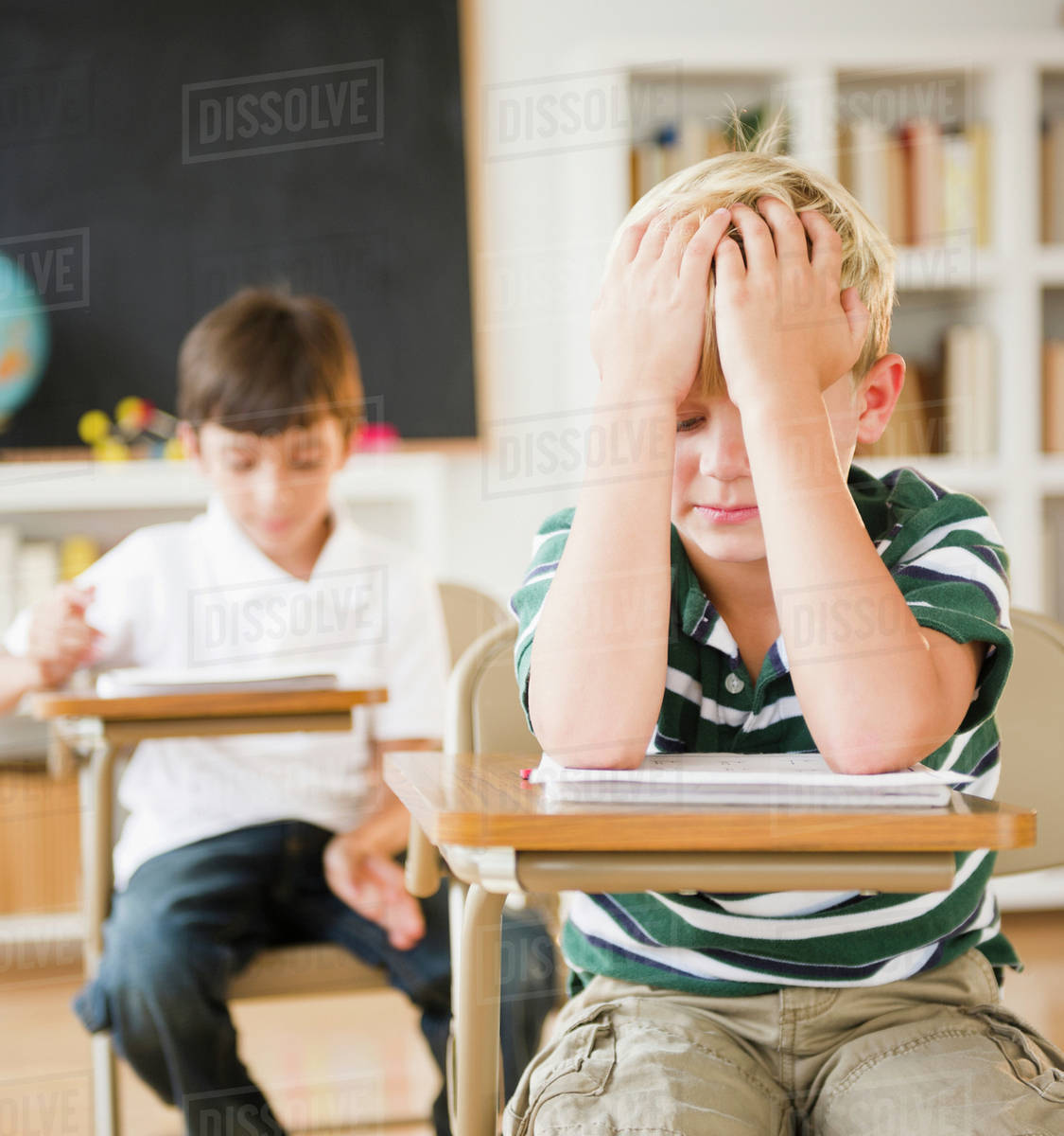 Frustrated Caucasian boy sitting at desk in classroom - Royalty-free ...