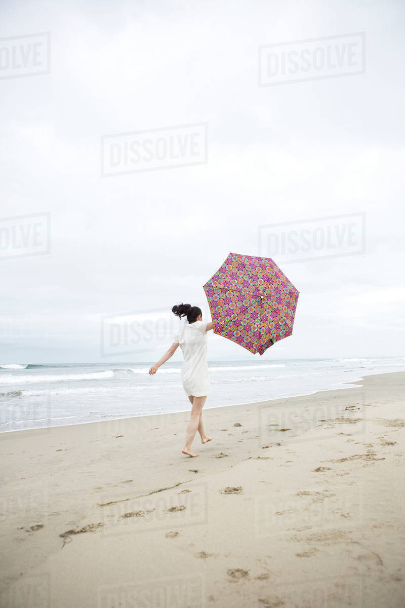 Woman walking in wind with umbrella on beach - Royalty-free Stock Photo ...