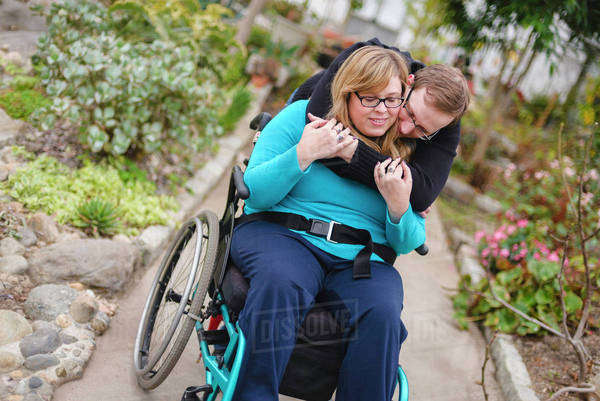 Man hugging paraplegic girlfriend in garden - Stock Photo - Dissolve
