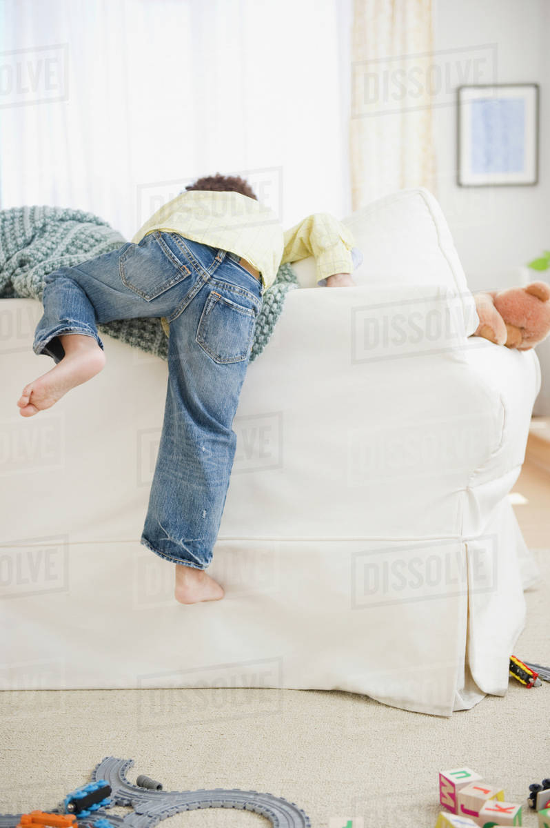 Black boy climbing over back of sofa - Stock Photo - Dissolve