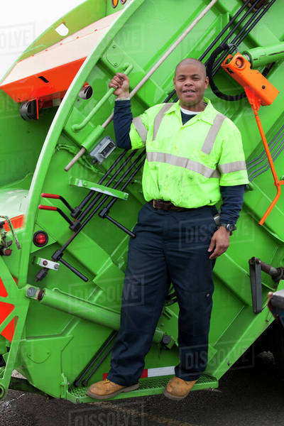 Black man riding on back of garbage truck - Stock Photo - Dissolve