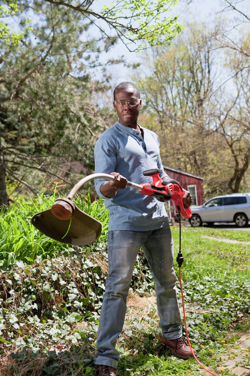 Black man holding weed trimmer - Stock Photo - Dissolve