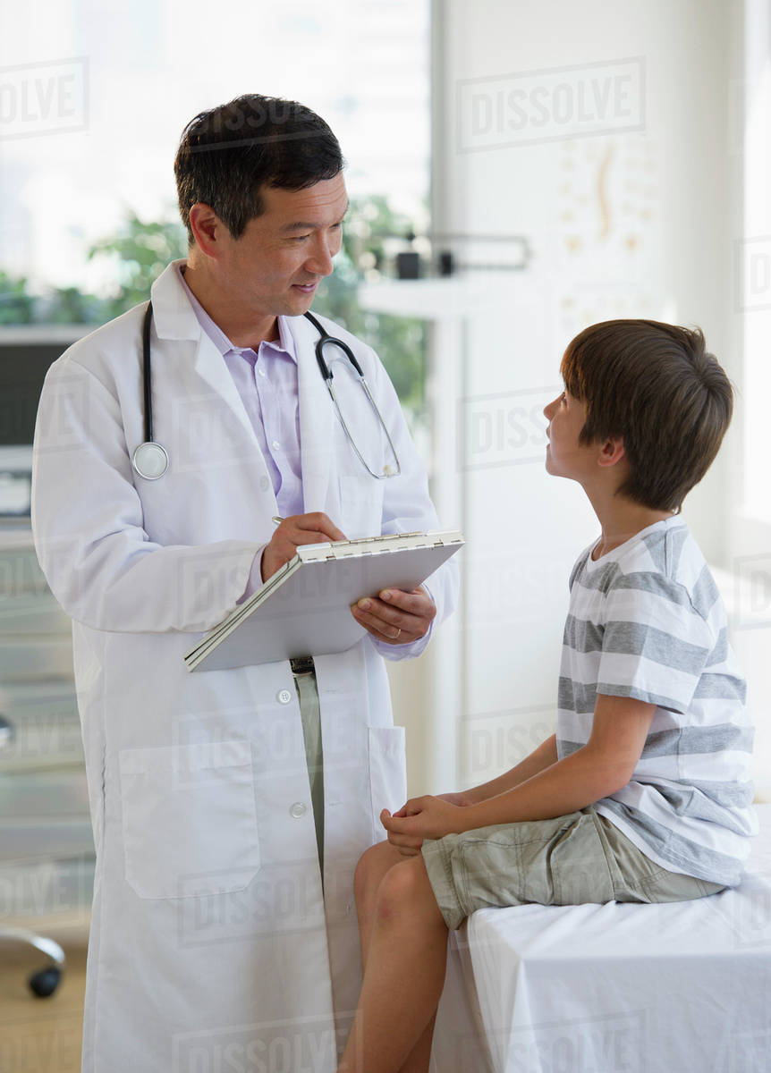 Doctor with medical chart talking to boy in examination room - Royalty ...