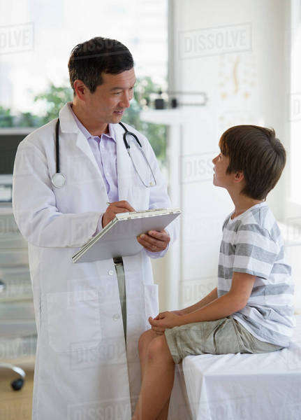 Doctor with medical chart talking to boy in examination room - Royalty ...