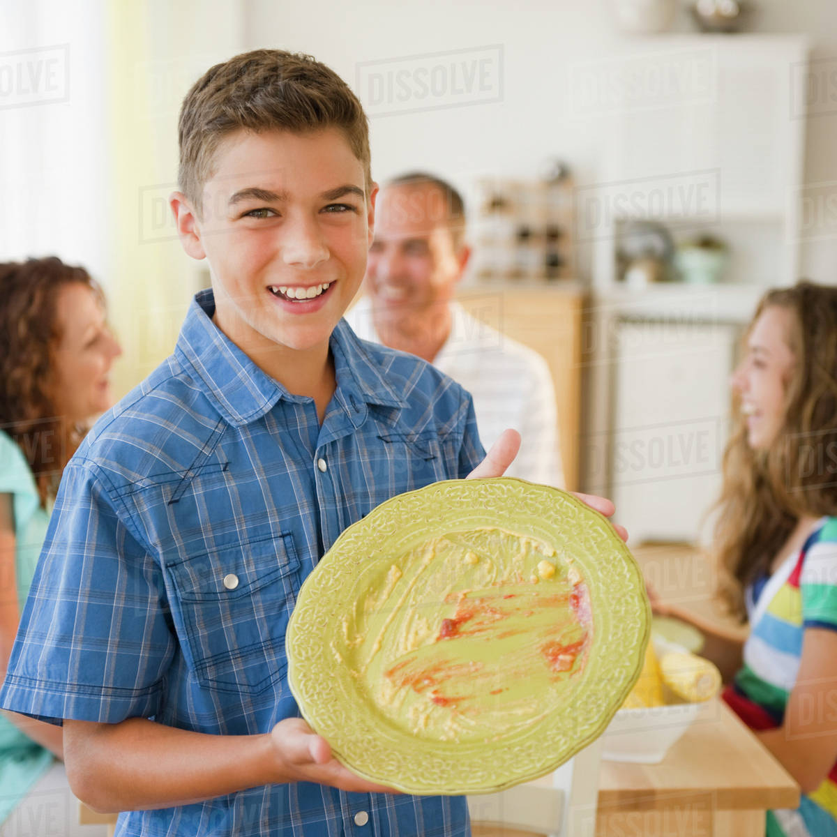 Smiling boy displaying empty plate with family at table in background ...