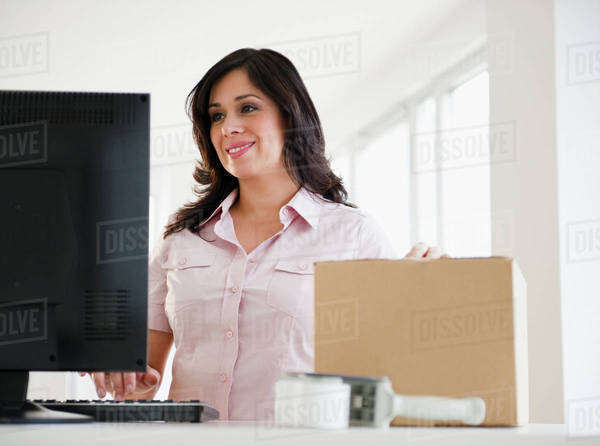 Smiling Hispanic woman with cardboard box using computer - Royalty-free ...