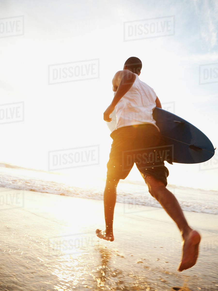Black man running with surfboard on beach - Stock Photo - Dissolve