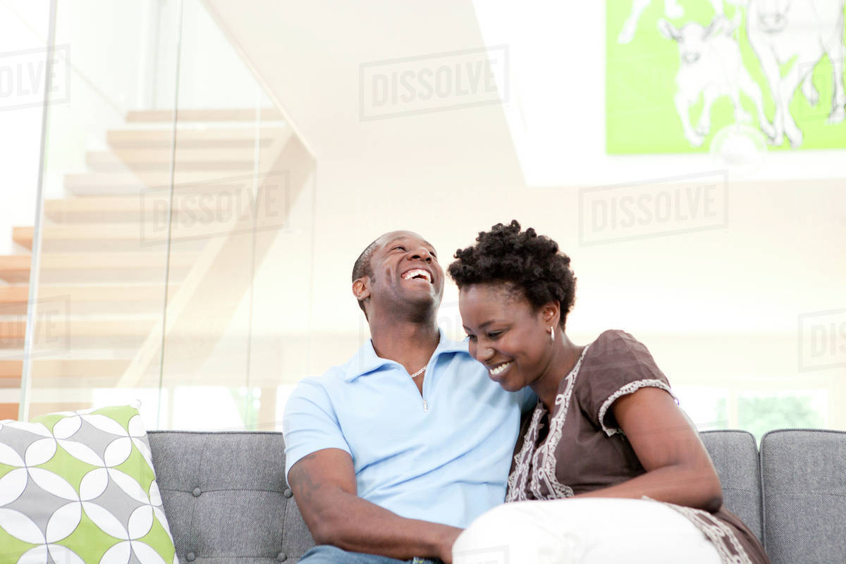 Laughing Black couple sitting on sofa in living room - Stock Photo ...