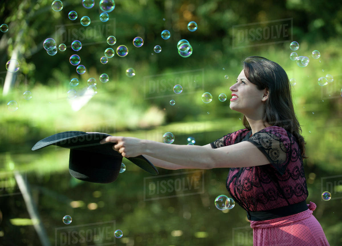 Caucasian woman trying to catch bubbles in hat - Stock Photo - Dissolve