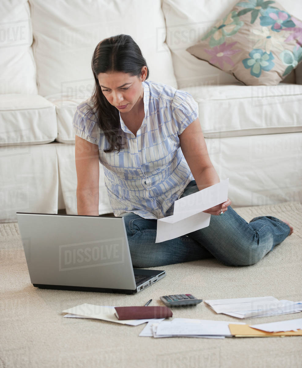 Hispanic woman paying bills with laptop on living room floor - Royalty ...