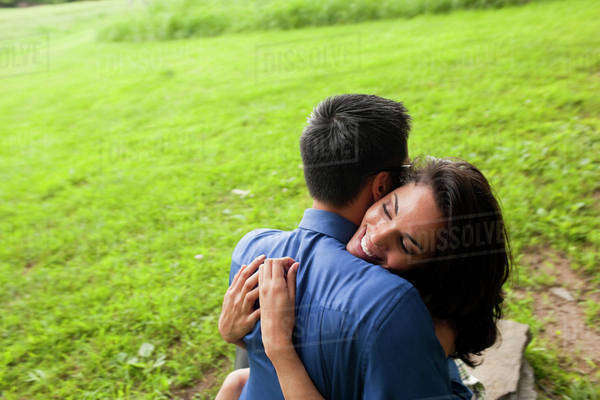 Hispanic couple hugging in field - Stock Photo - Dissolve