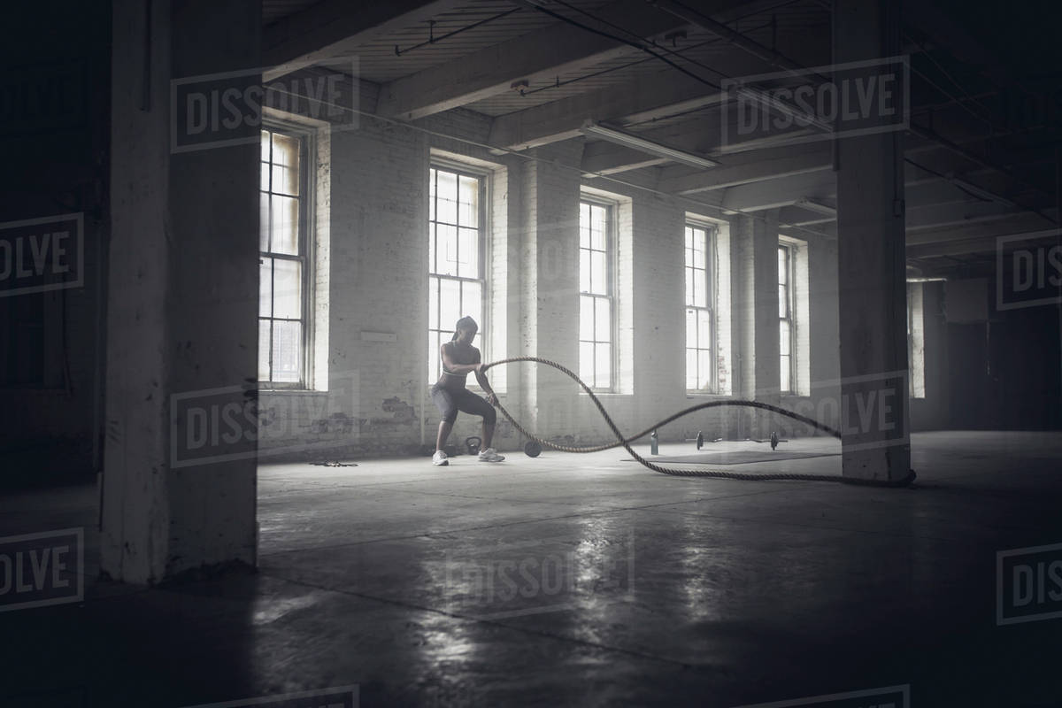 Black woman tossing ropes in dark gym - Royalty-free Stock Photo | Dissolve