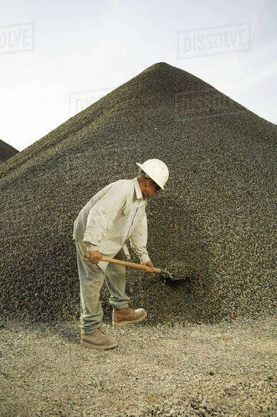 Hispanic man shoveling gravel - Stock Photo - Dissolve