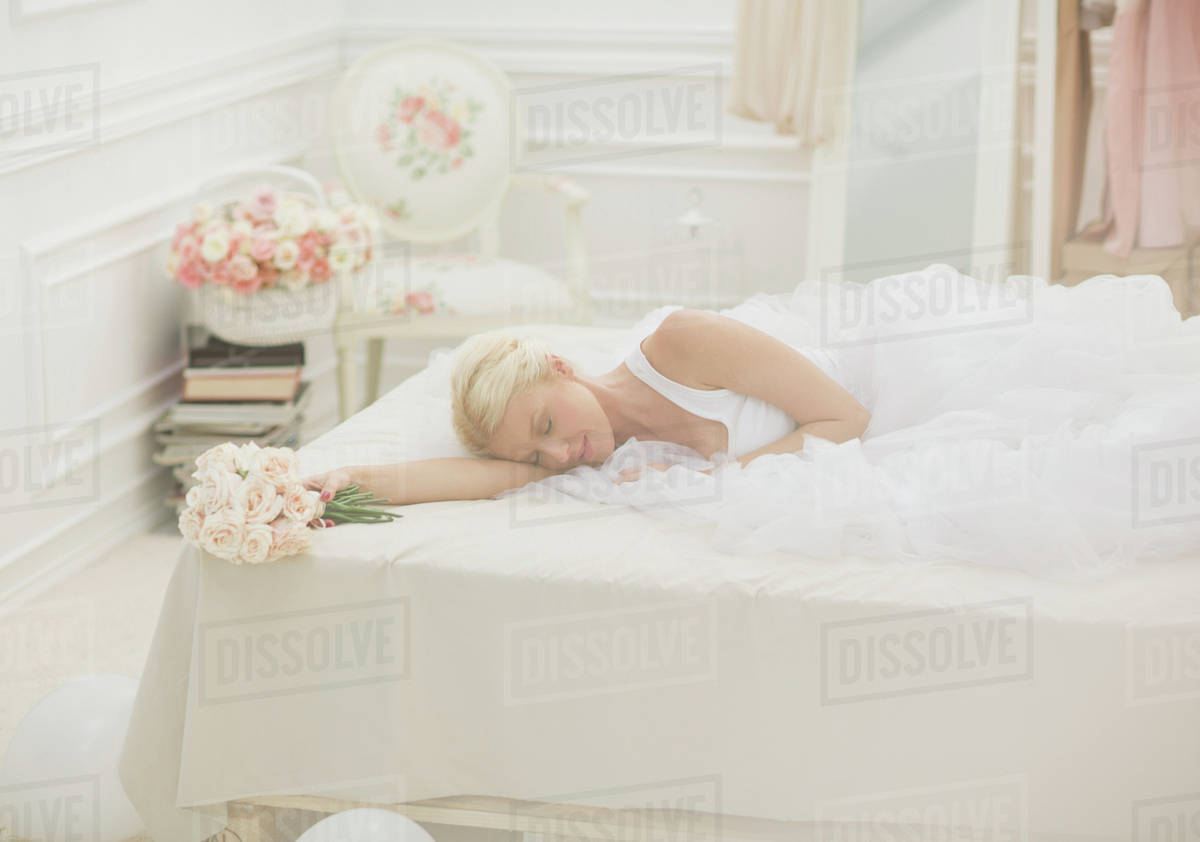 Bride sleeping on bed with bouquet of flowers - Stock Photo - Dissolve