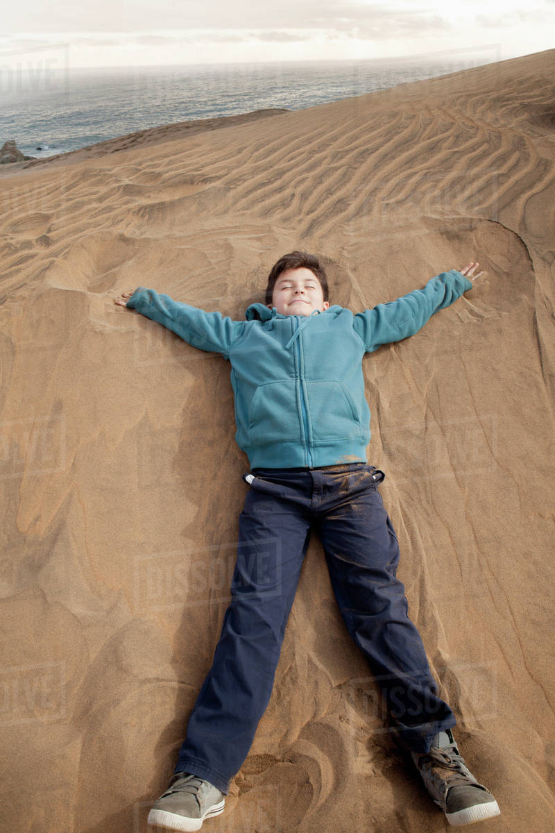 Hispanic boy laying on sand dune at beach - Royalty-free Stock Photo ...