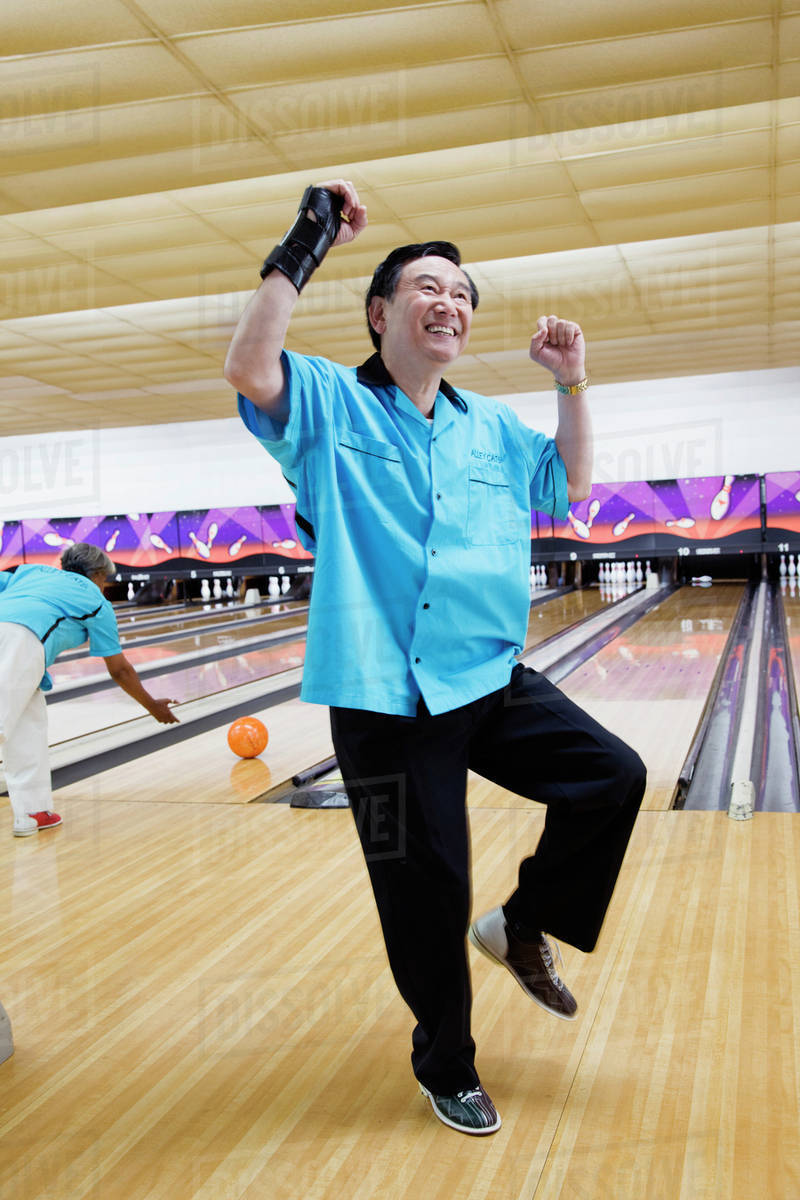 Asian man cheering in bowling alley - Stock Photo - Dissolve