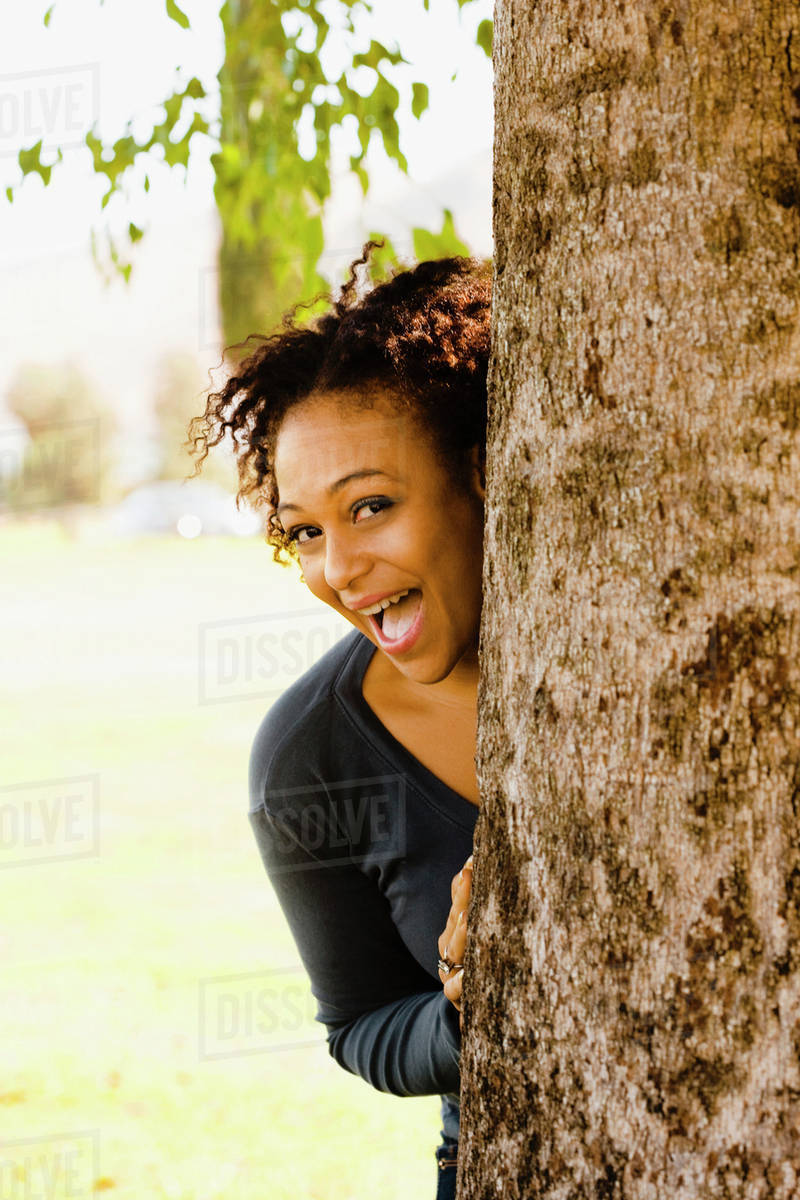Playful African woman behind tree - Royalty-free Stock Photo | Dissolve