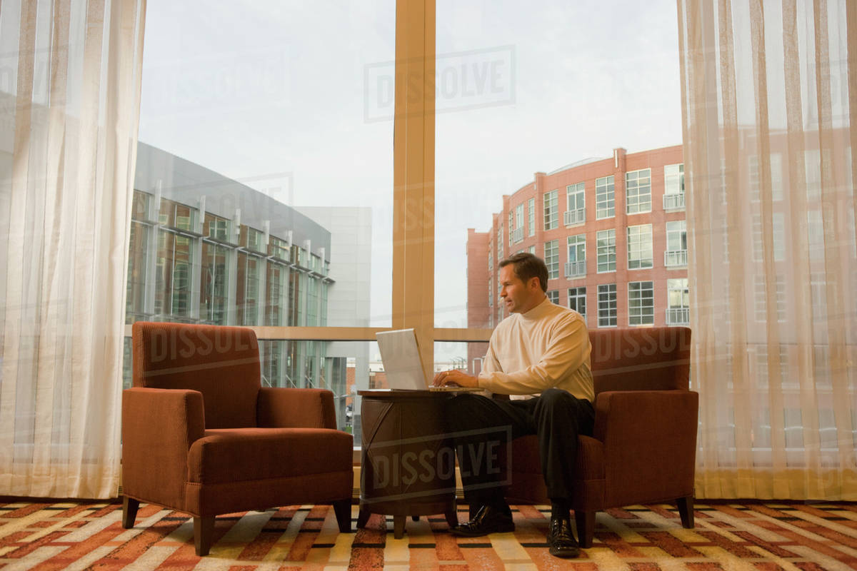 Businessman working on laptop in hotel waiting area - Stock Photo ...