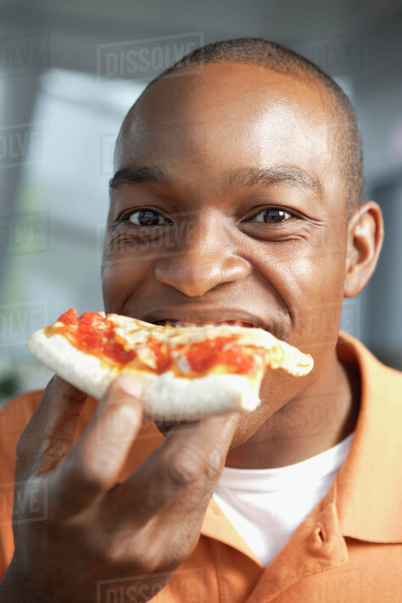 Close up of African man eating pizza - Royalty-free Stock Photo | Dissolve