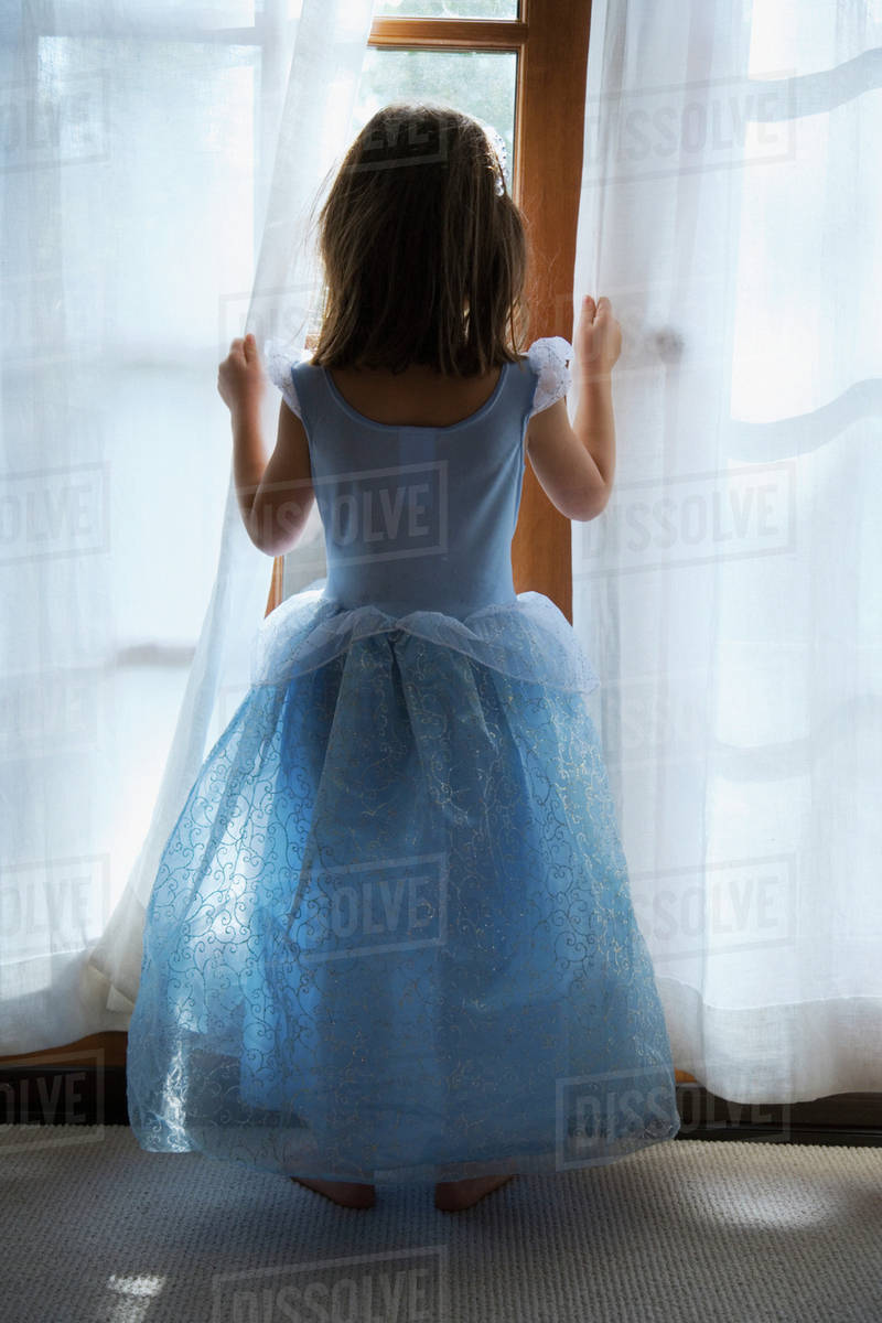 Rear view of girl dressed as princess and looking out window - Stock ...